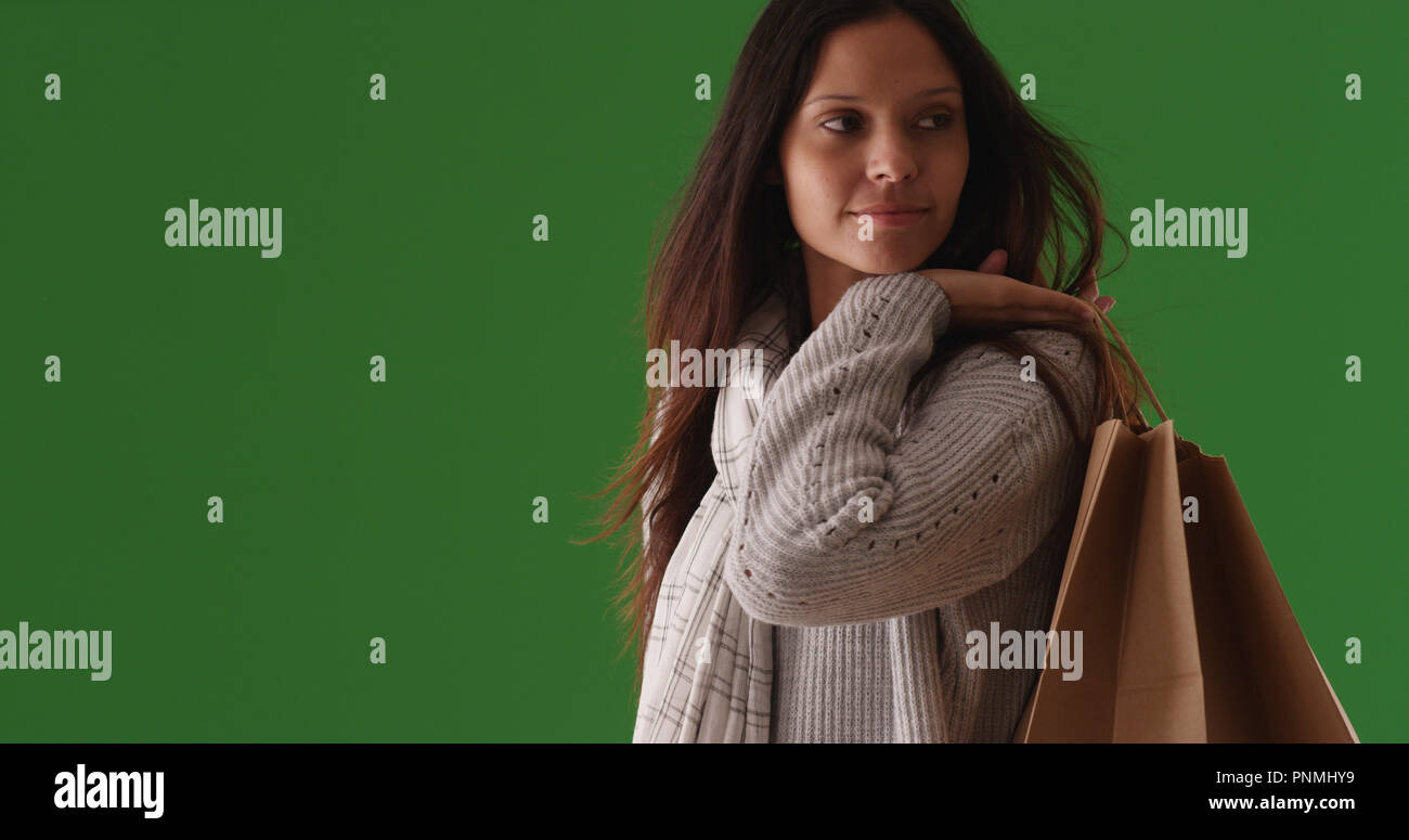 Portrait of young woman carrying shopping bags over shoulder on green ...