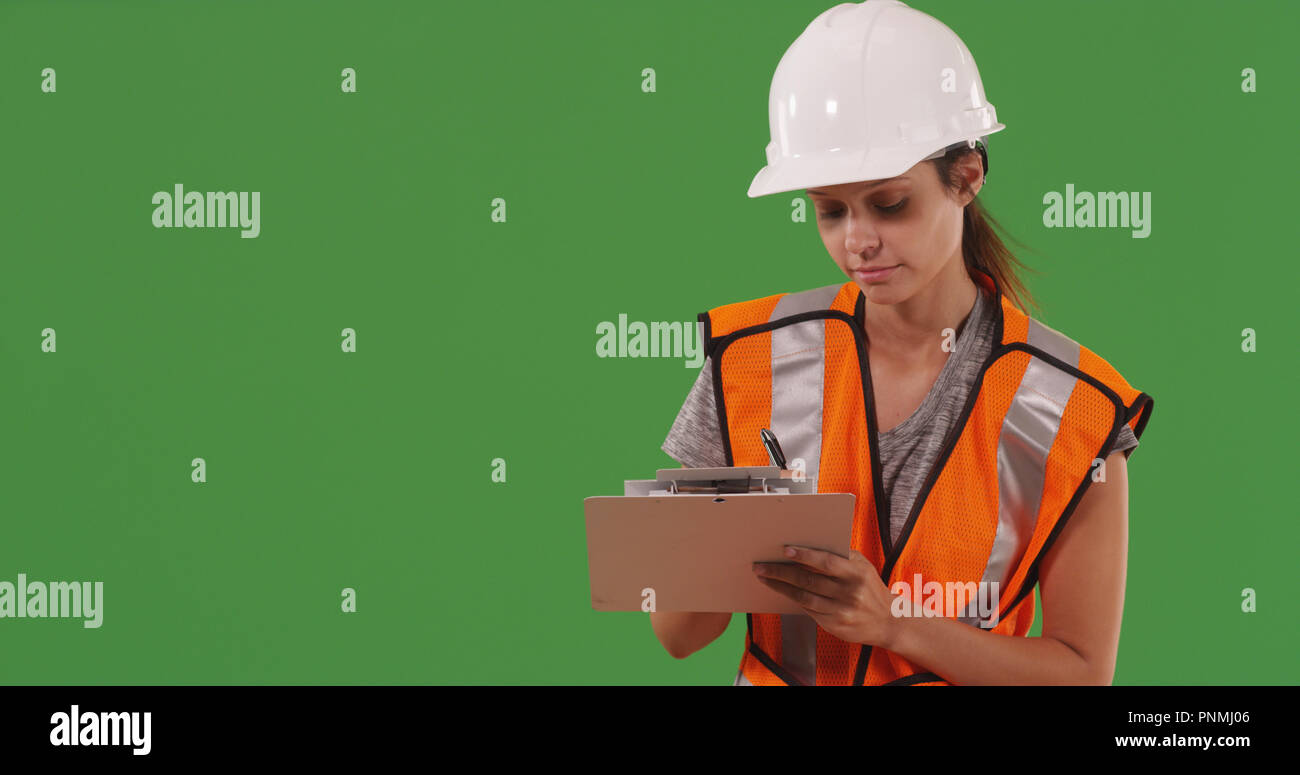 Female construction worker writing notes on clipboard on green screen ...