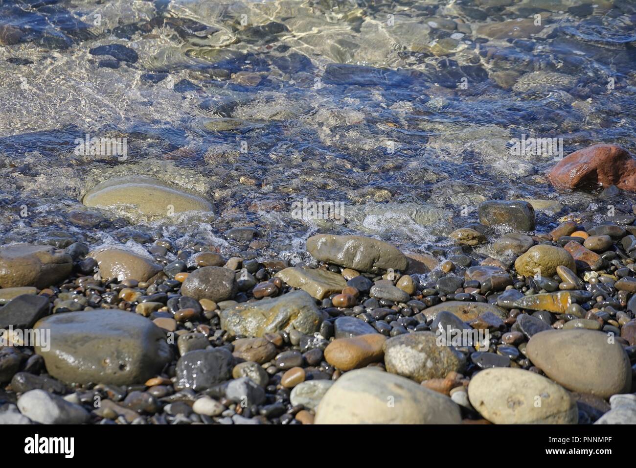Rock and pebble strewn beach with sea water approaching Stock Photo - Alamy