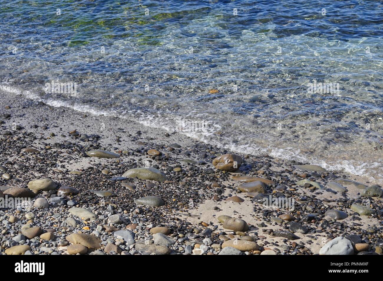 Pebbles, of various sizes, on a sandy beach with the water approaching ...