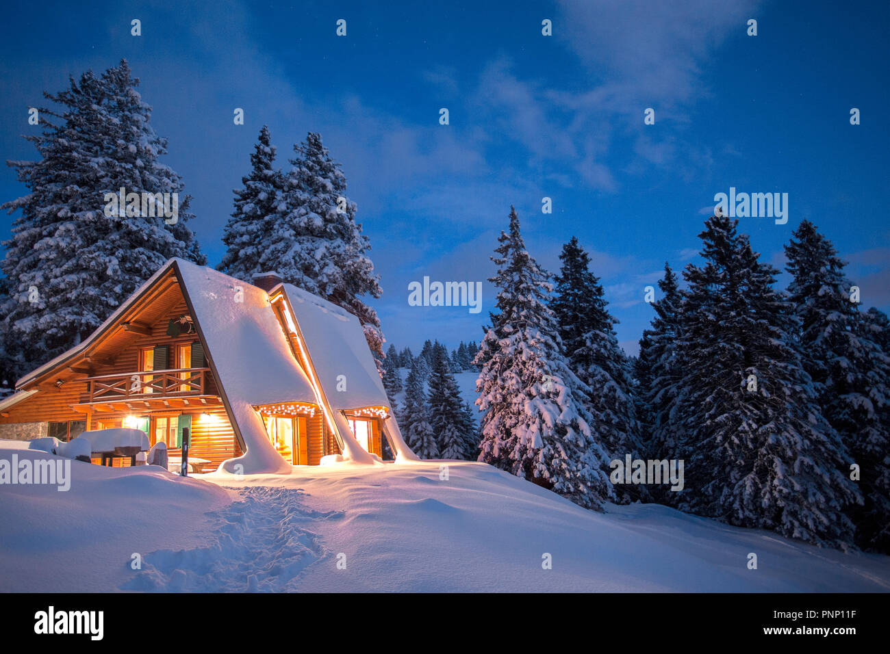 Solitary wooden mountain hut with lights in the snow at sunset in ...