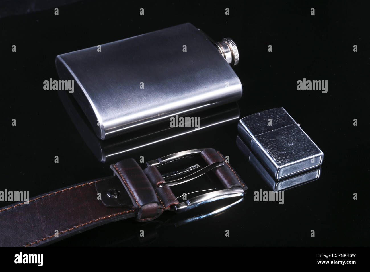 Stainless hip flask, lighter and luxury belt isolated on mirror black ...