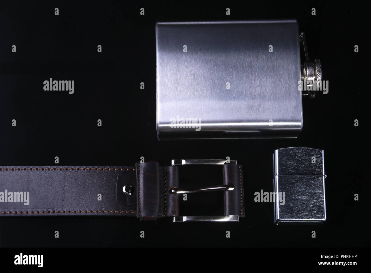 Stainless hip flask, lighter and luxury belt isolated on mirror black ...
