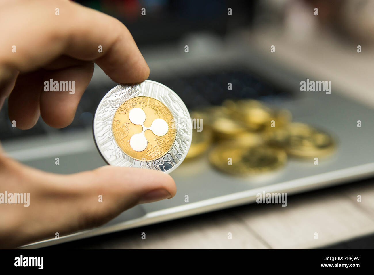 Male businessman hand holding Ripple coin on a background of laptop ...
