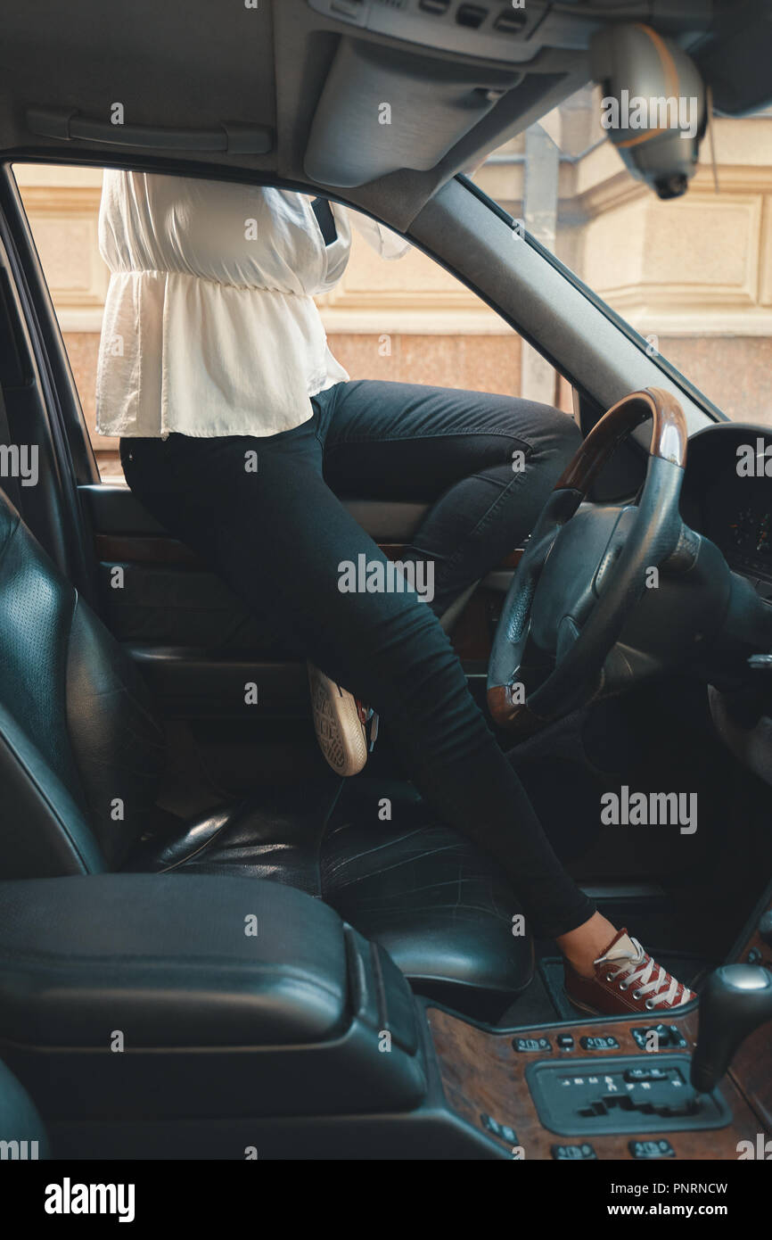 A cropped image of a woman sitting on the car window with crossed legs ...