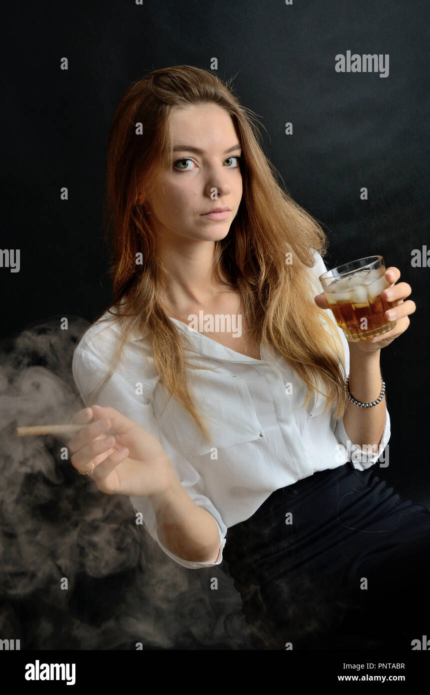 Young female sits with cigarillo and glass of whiskey in her hand ...