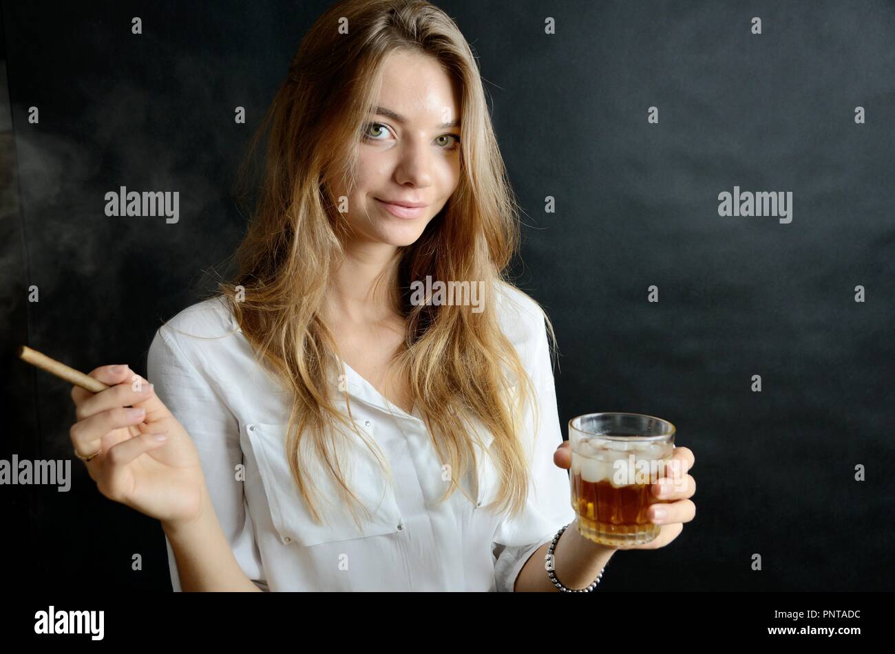 Young female sits with cigarillo and glass of whiskey in her hand ...