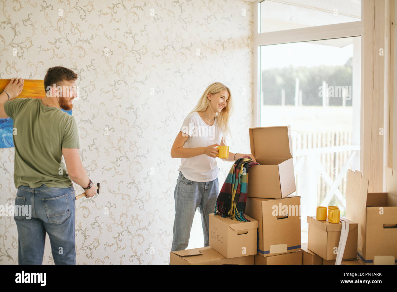 Moving house. Couple hanging picture on wall in new home Stock Photo ...