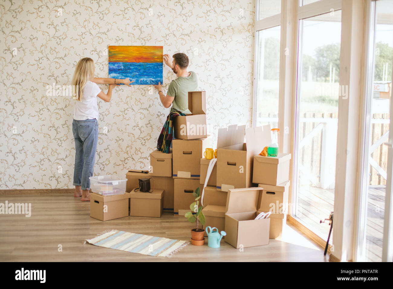 Moving house. Couple hanging picture on wall in new home Stock Photo ...