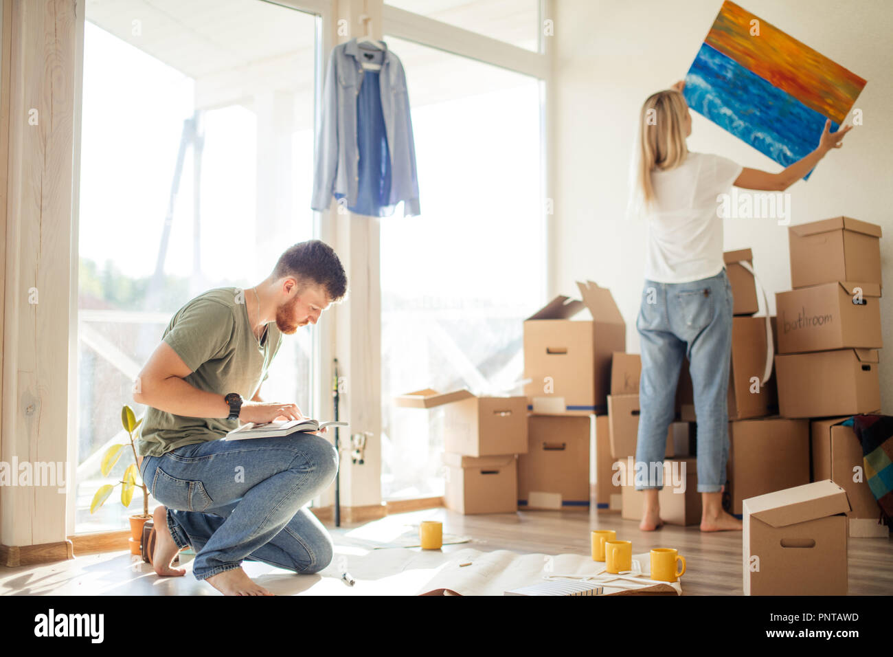 Moving house. Couple hanging picture on wall in new home Stock Photo ...