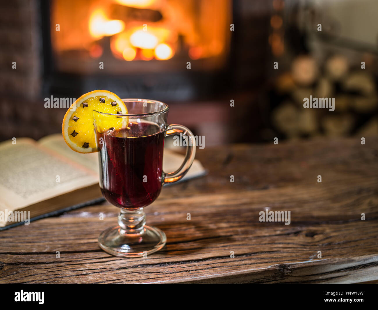 Hot mulled wine and a book on the wooden table. Fireplace with warm ...
