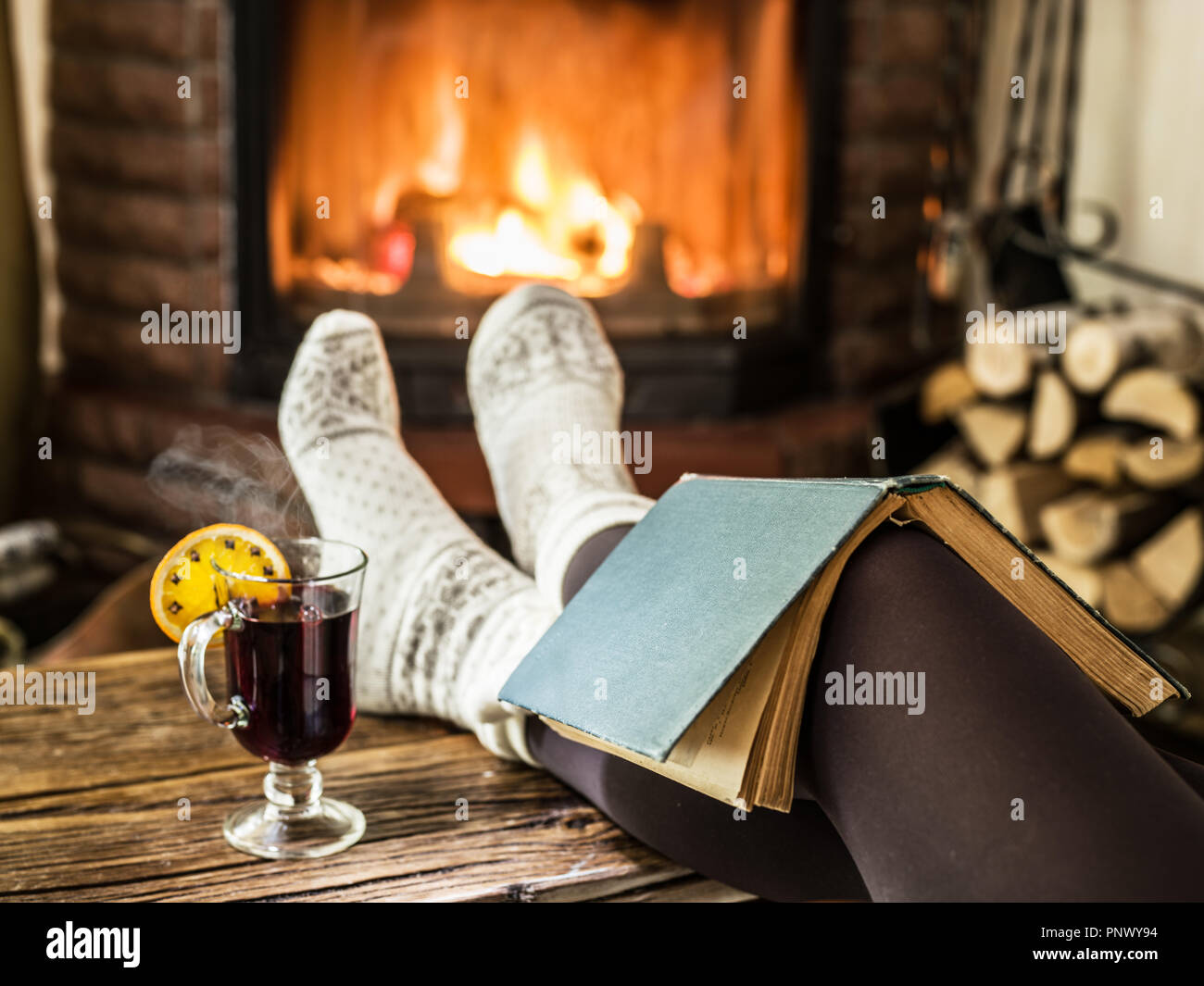 Hot mulled wine and book in woman hands. Relaxing in front of burning ...
