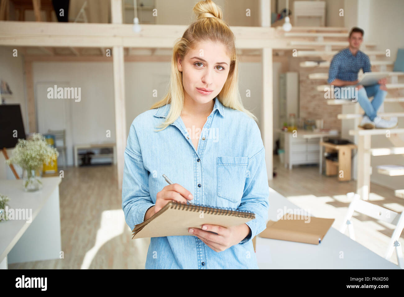 Pretty young blonde businesswoman making notes in notepad while ...