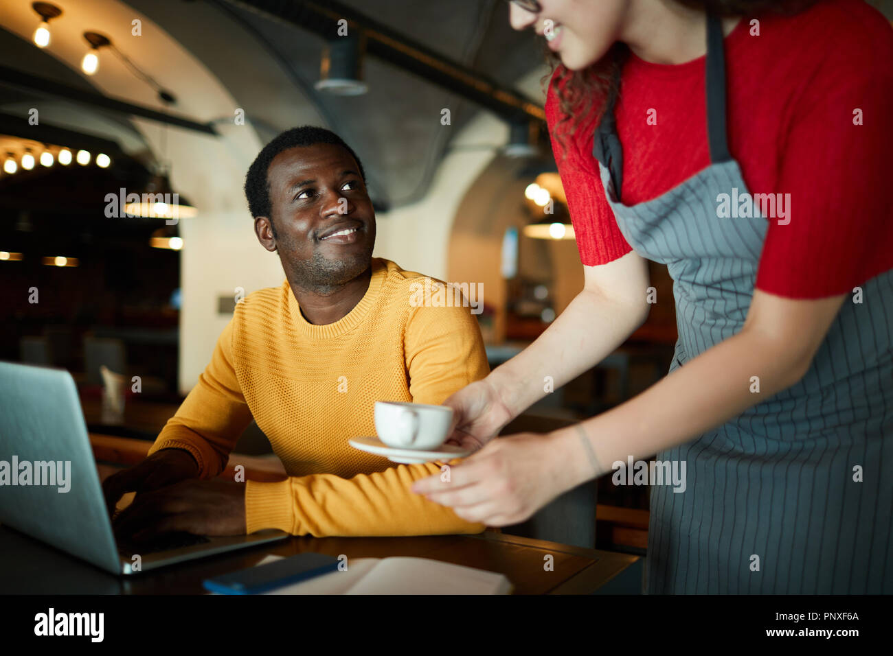 African-american guy looking at young waitress bringing him cup of tea ...