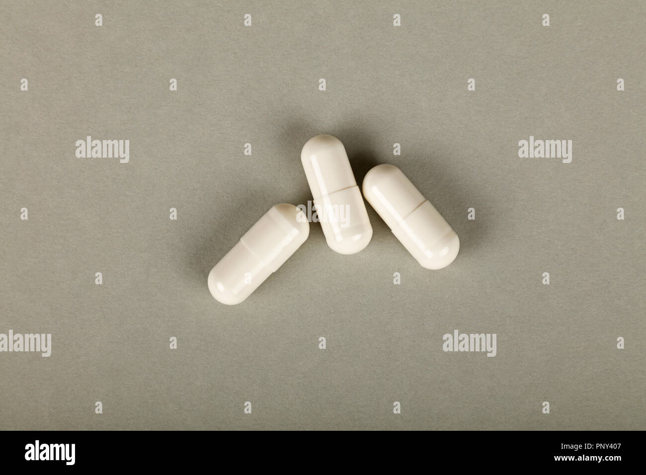 Close up three white gel cap pills of medicine over grey background ...