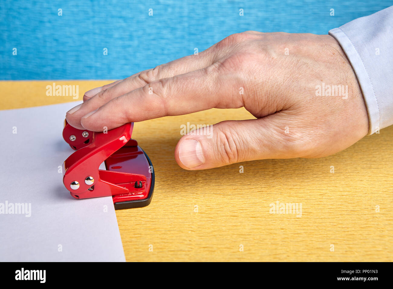 Office worker punching holes in sheet of paper, using red steel hole ...