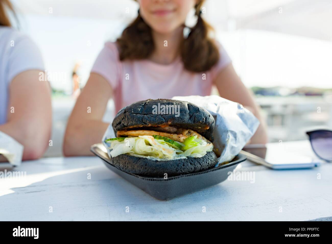 Close-up of black fast food burger. Background girls teenagers, outdoor ...