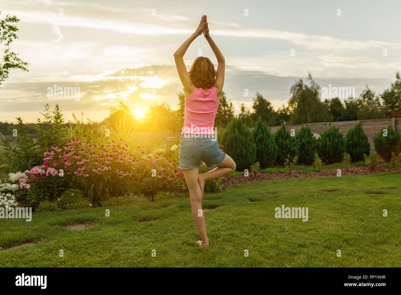 Young girl practicing yoga, meditating on a summer sunset background ...