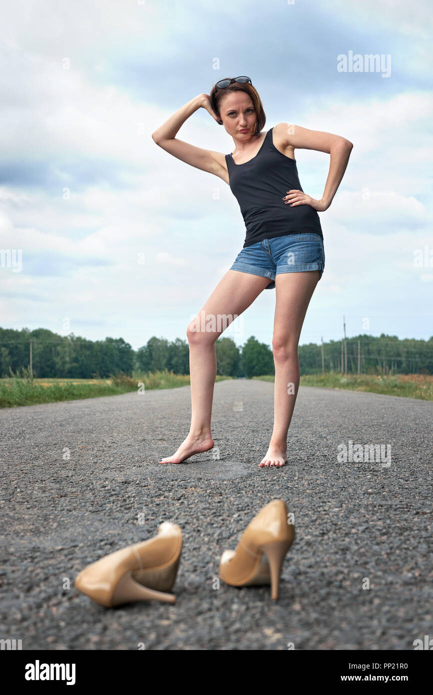 young girl walking barefoot on the road, she left her shoes on the road ...