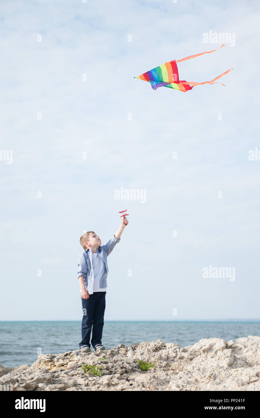 healthy small kid holding flying colorful kite on autumn sea horizon ...