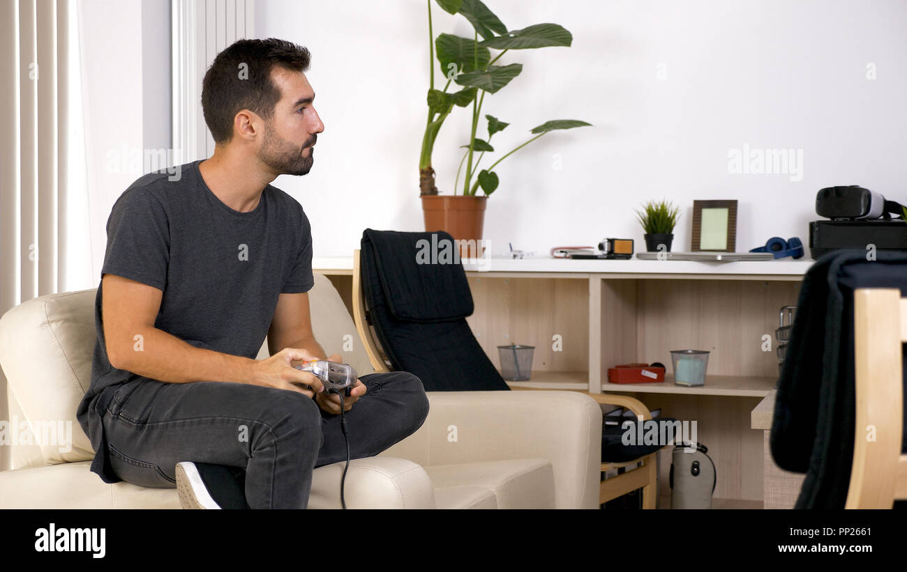 Attractive young man sitting on his couch and playing video games ...