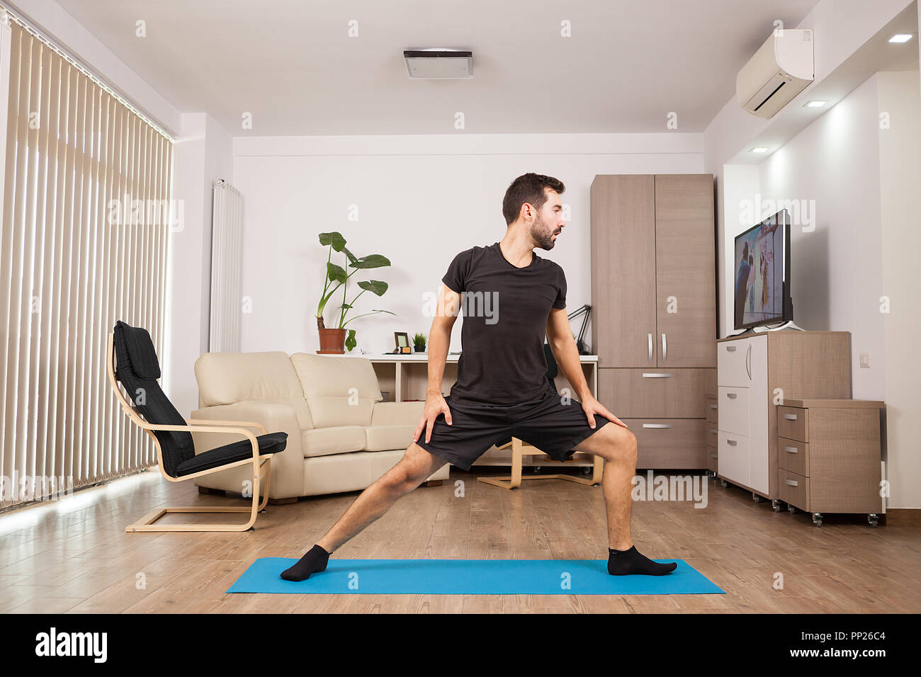 Bearded man doing Warrior II yoga posing and stretching his muscles ...