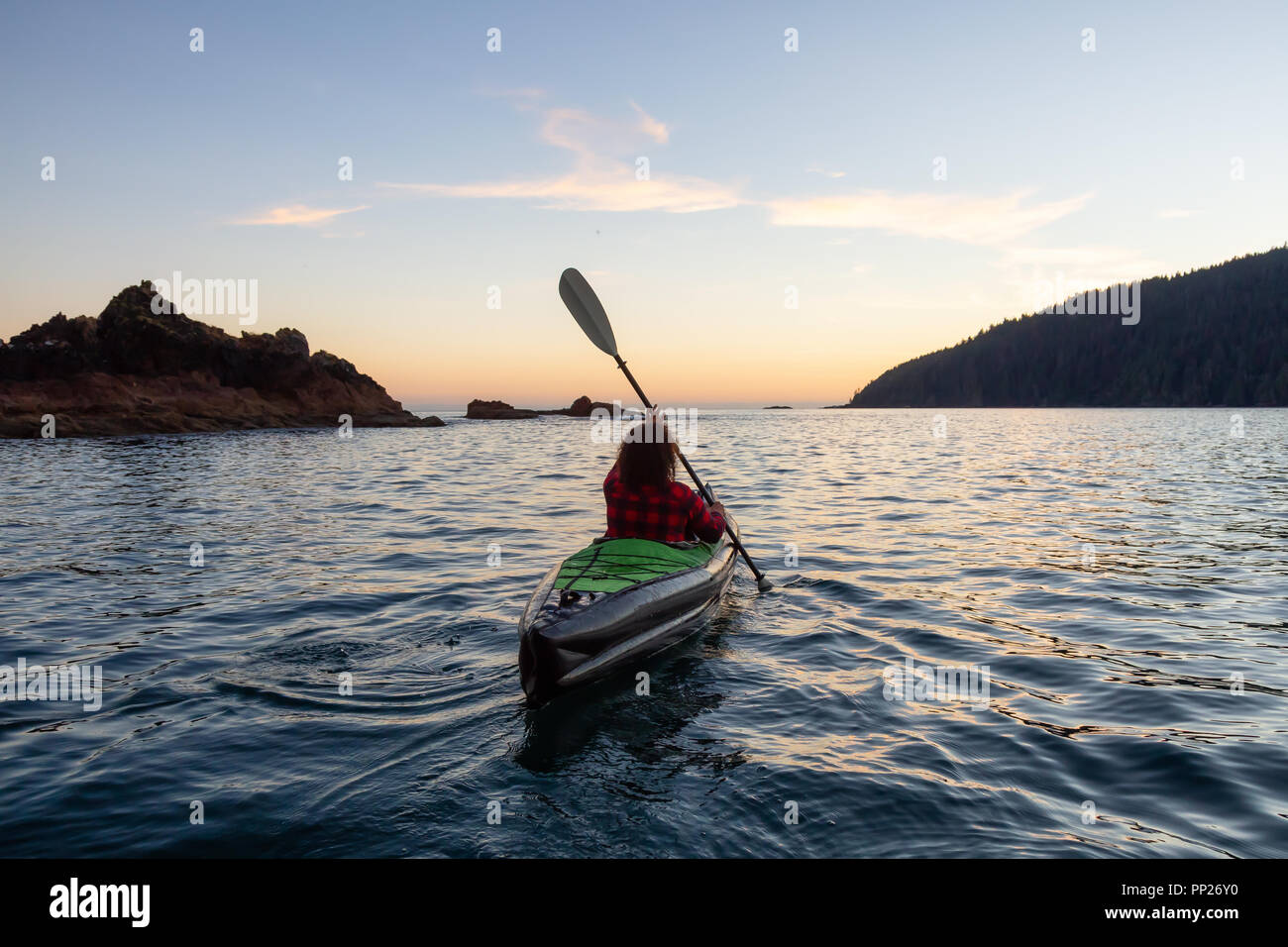 Girl kayaking in the Pacific Ocean during a cloudy summer sunset. Taken ...