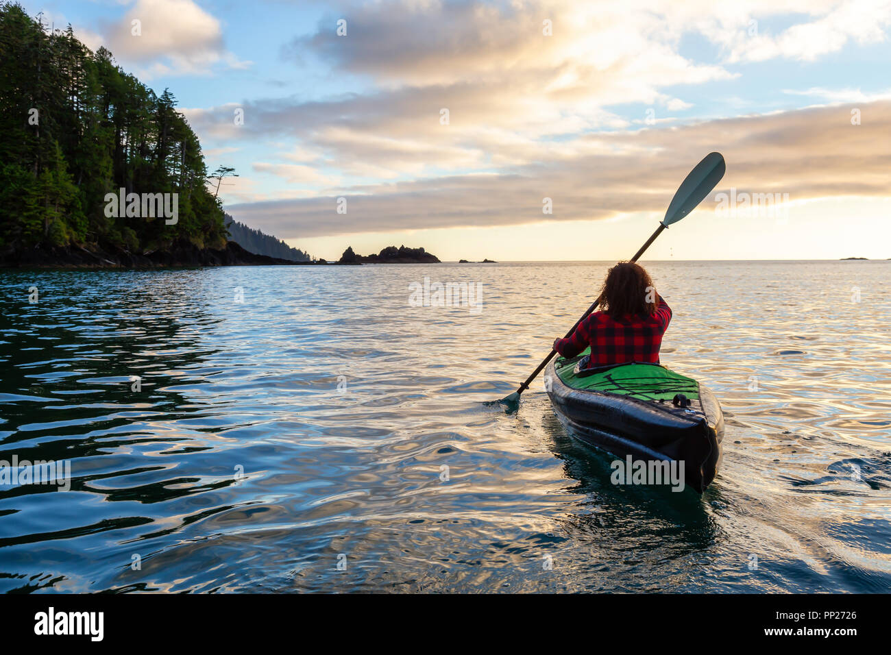 Girl kayaking in the Pacific Ocean during a cloudy summer sunset. Taken ...