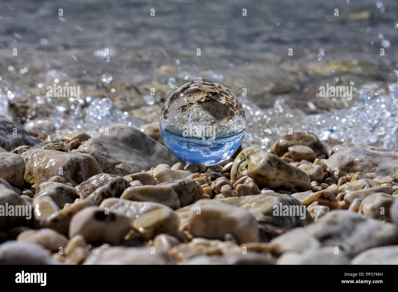 Glass ball sitting at rocky beach whit sea wave reflected in it ...