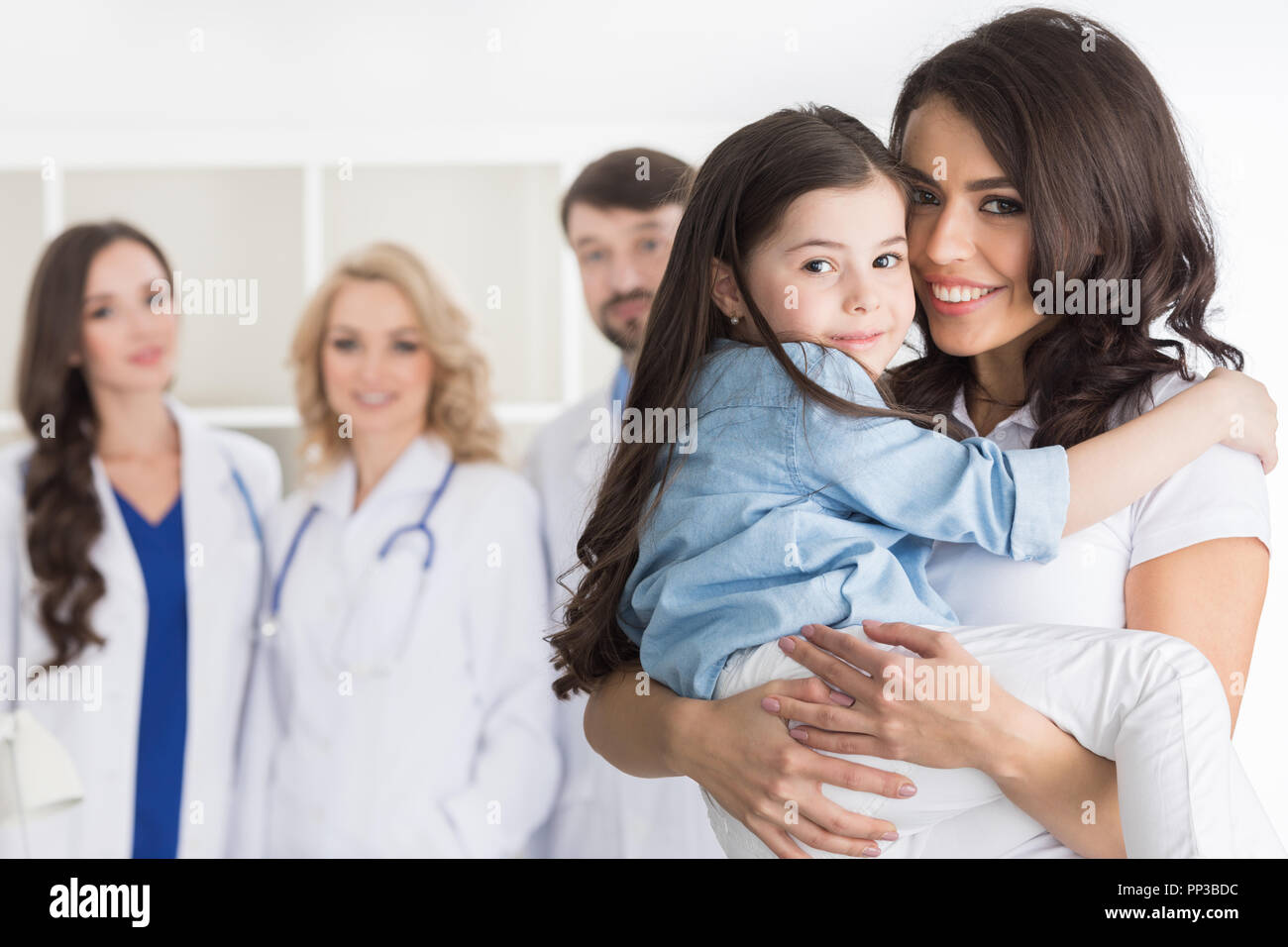 Mother and daughter in medical clinic, team of doctors on background ...