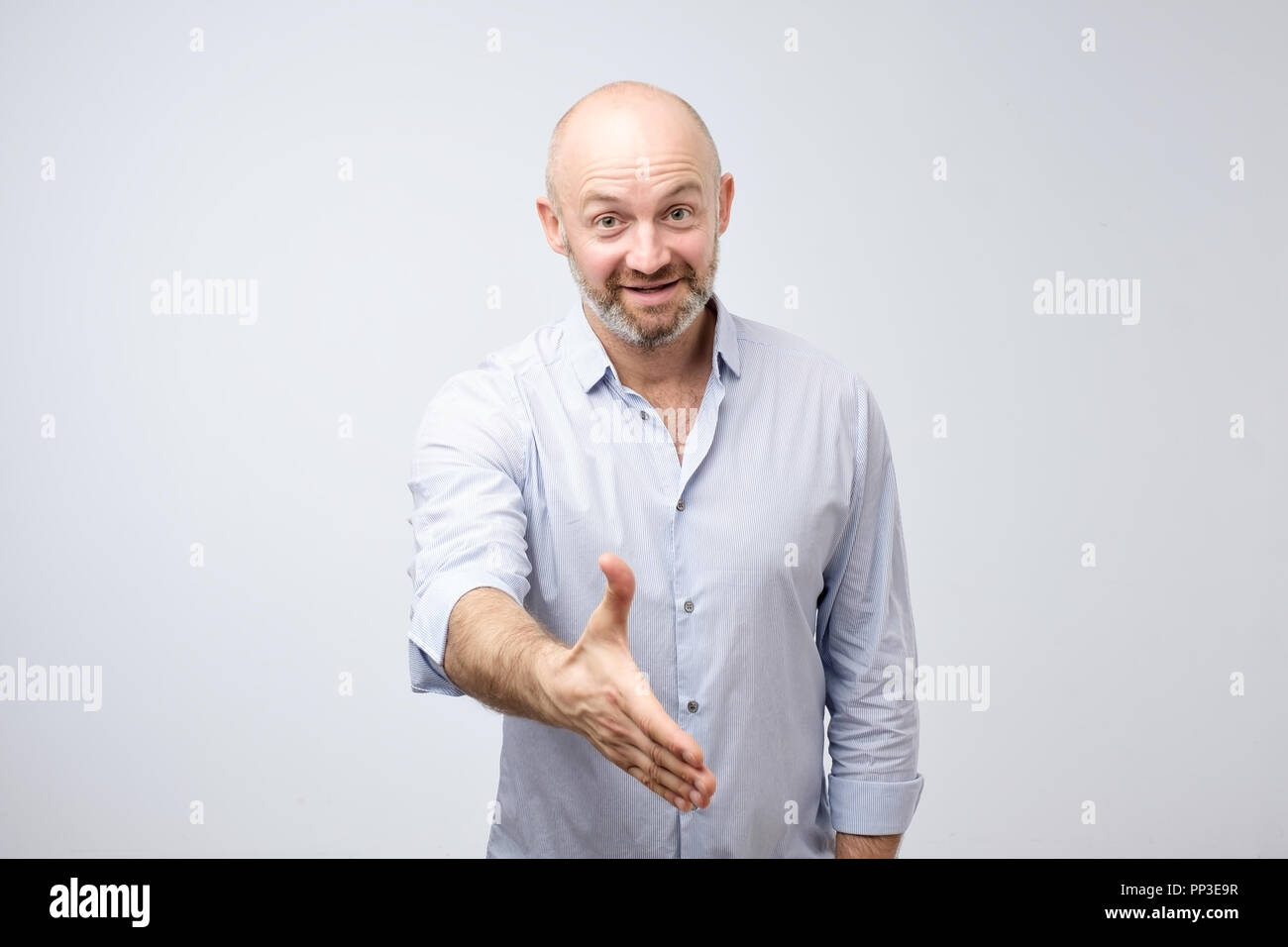 Friendly-looking attractive european man giving a hand in hello gesture ...