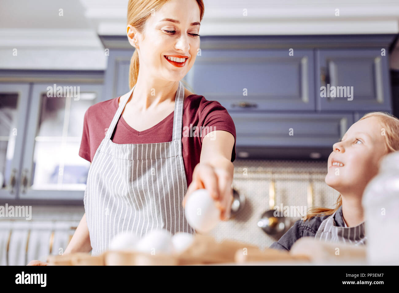 Beautiful woman with red lips smiling to her daughter while cooking ...