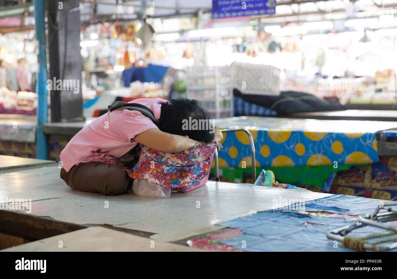 An tired old woman having a short nap in the market stall in Chiang Mai ...