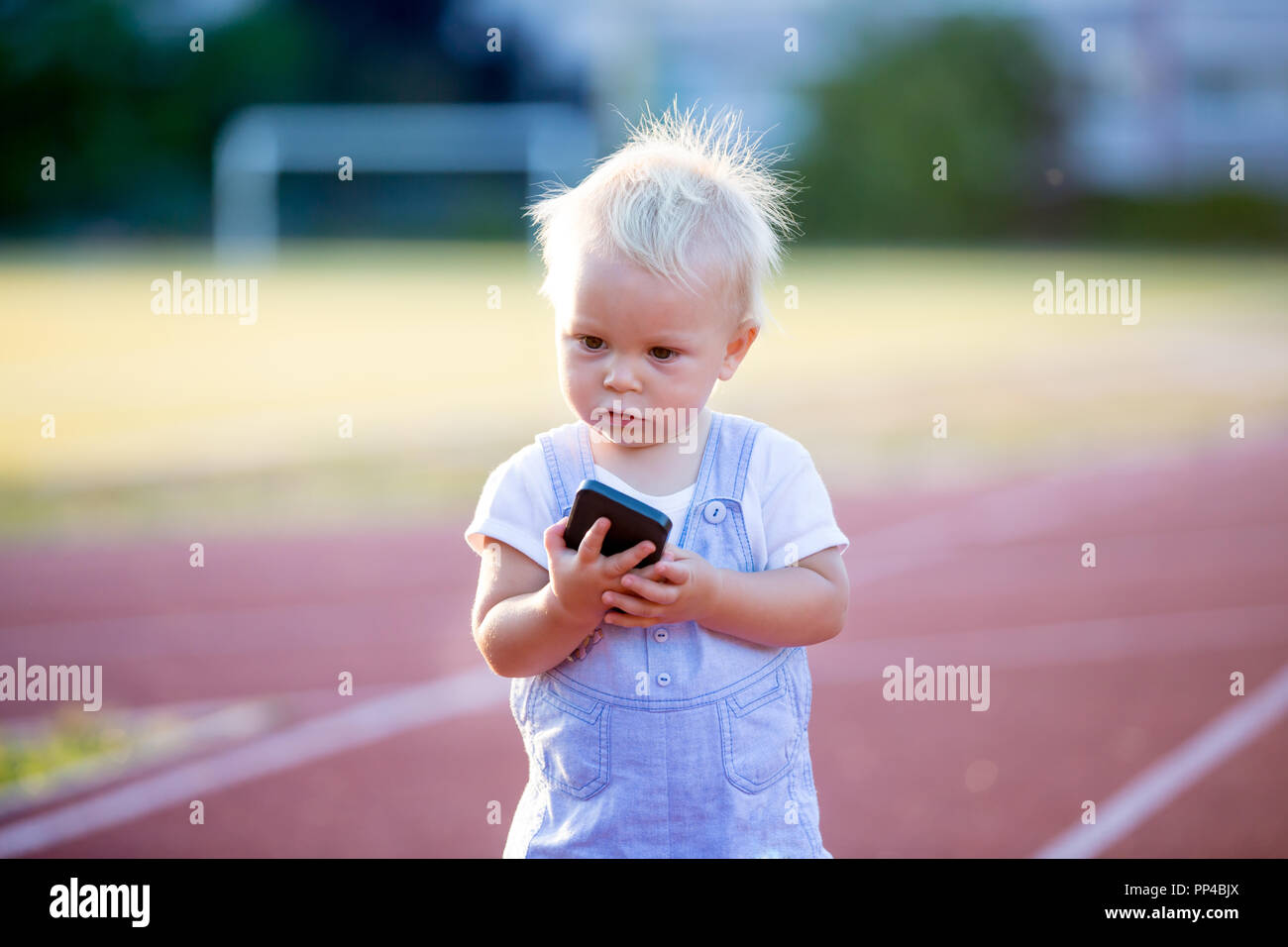 Cute baby boy playing with mobile phone in the park, digital ...