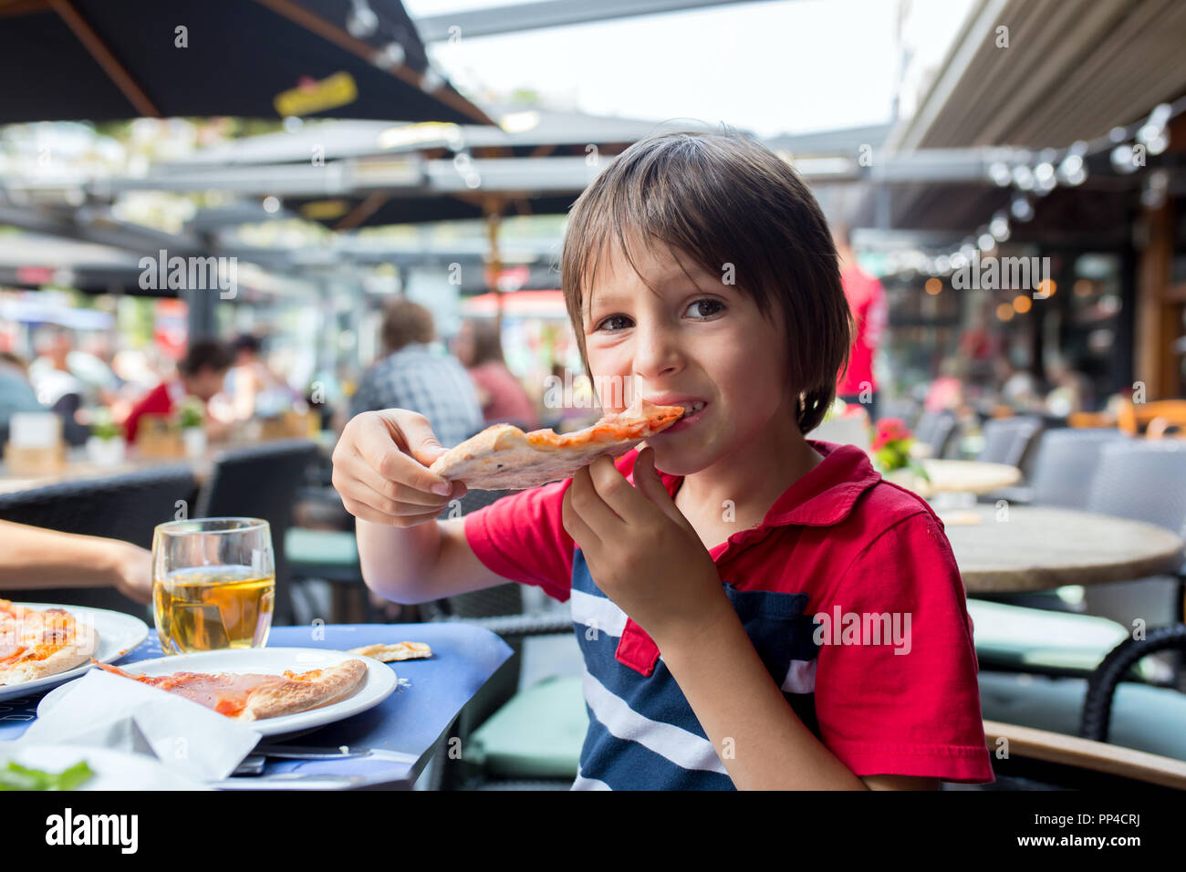 Cute child, boy, eating pizza in restaurant, happily smiling and biting ...