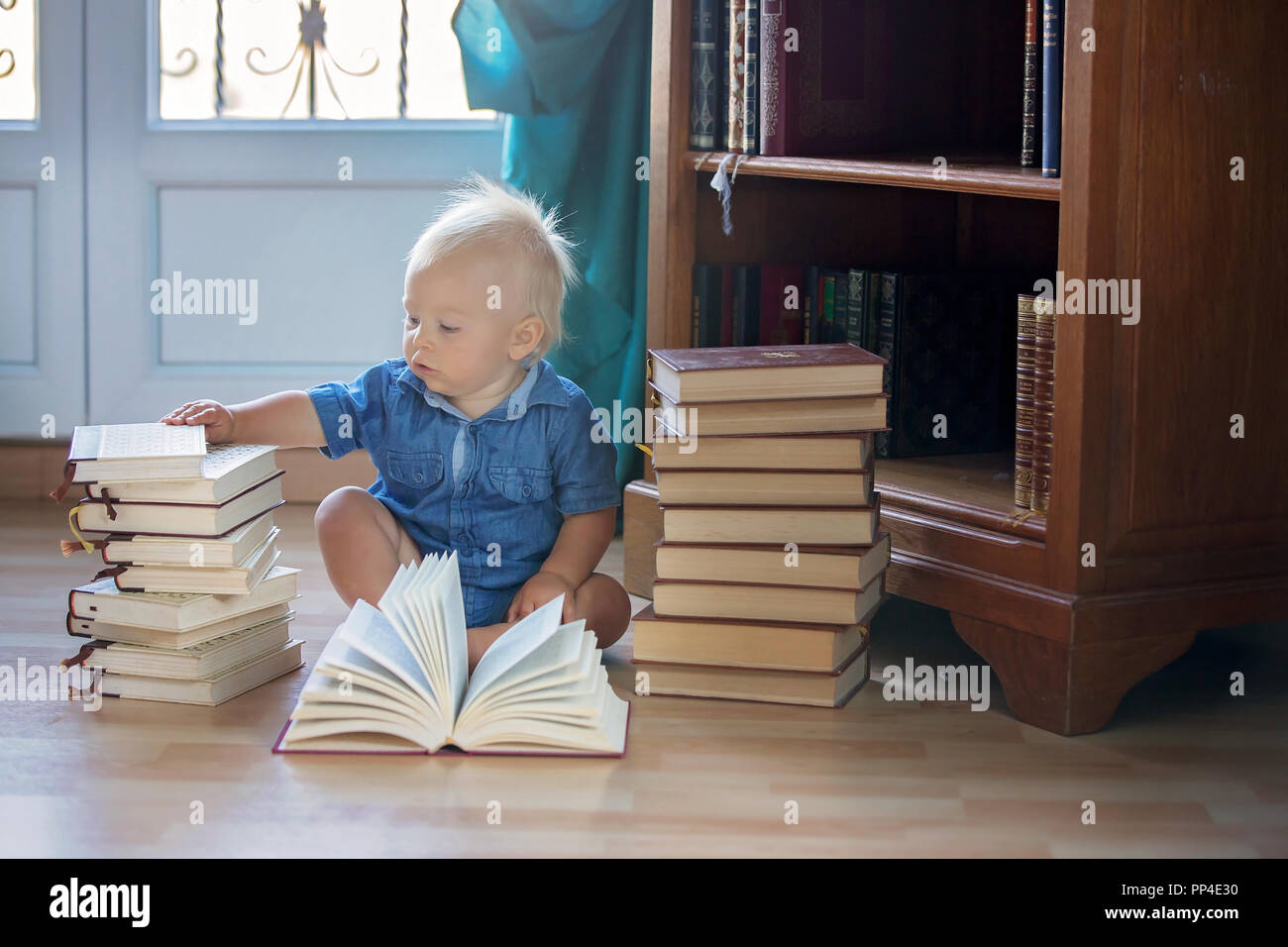 Baby child reading a book at home. Boy studying on blue background ...