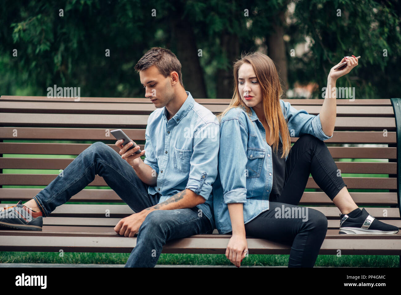 Phone addiction, young couple on the bench in park. Man and woman using ...