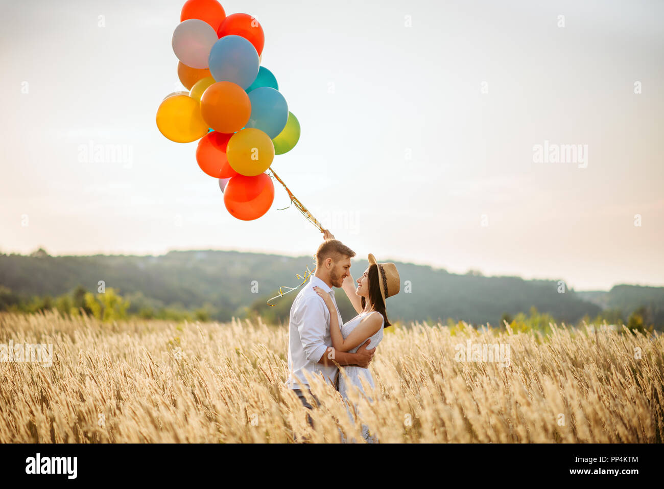 Love couple with colorful air balloons in a rye field. Pretty woman on ...