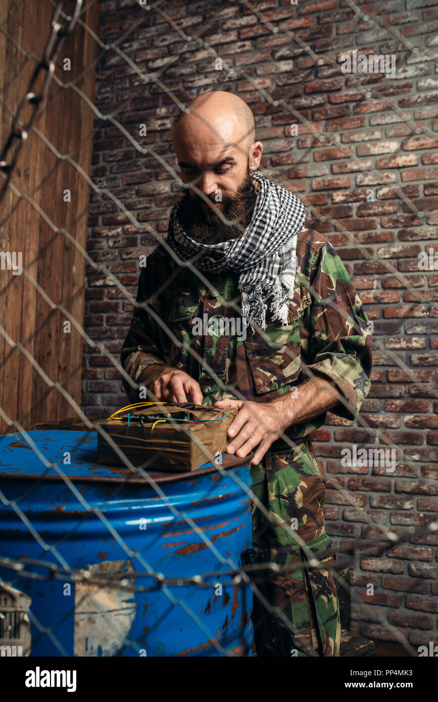 Bearded terrorist in uniform sets the bomb on the barrels of fuel or ...