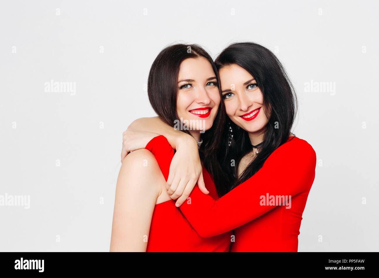 Beautiful smiling sisters in red embracing over white background Stock ...
