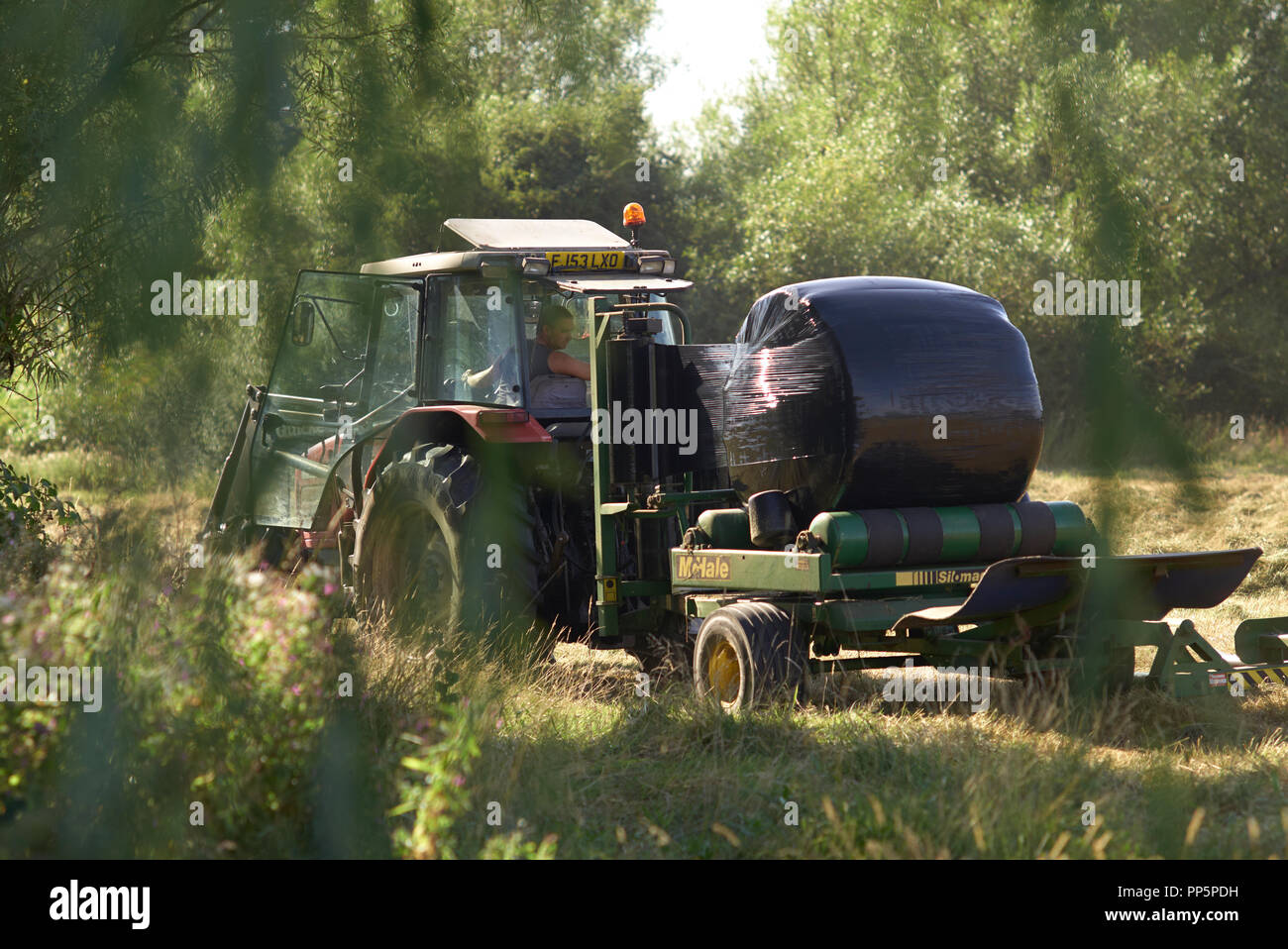 Tractor wrapping bales in black plastic Stock Photo - Alamy