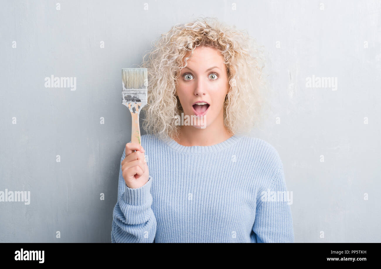 Young blonde woman with curly hair over grunge grey background holding ...