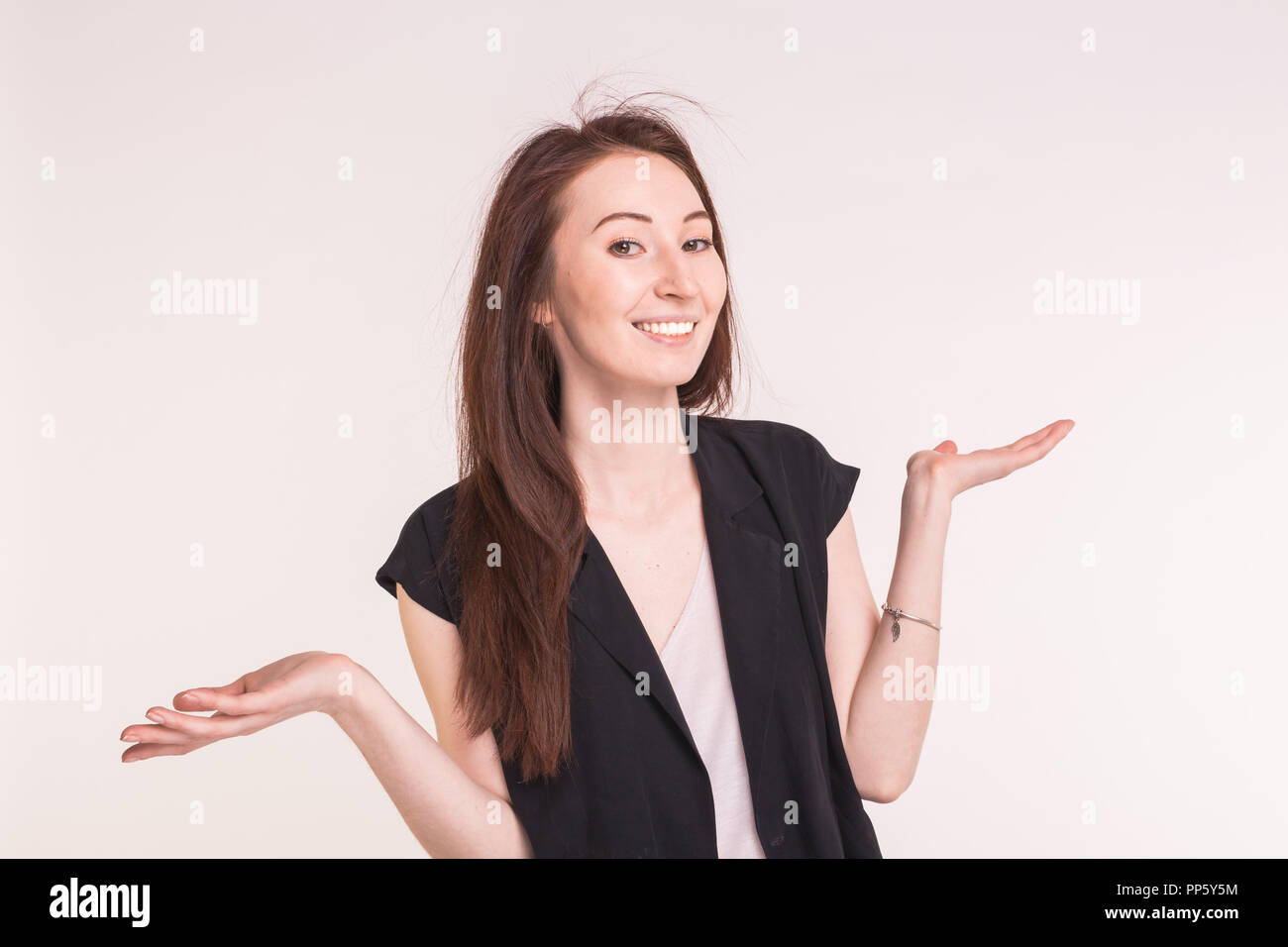 Young brunette asian woman is shrugging her shoulders on white ...