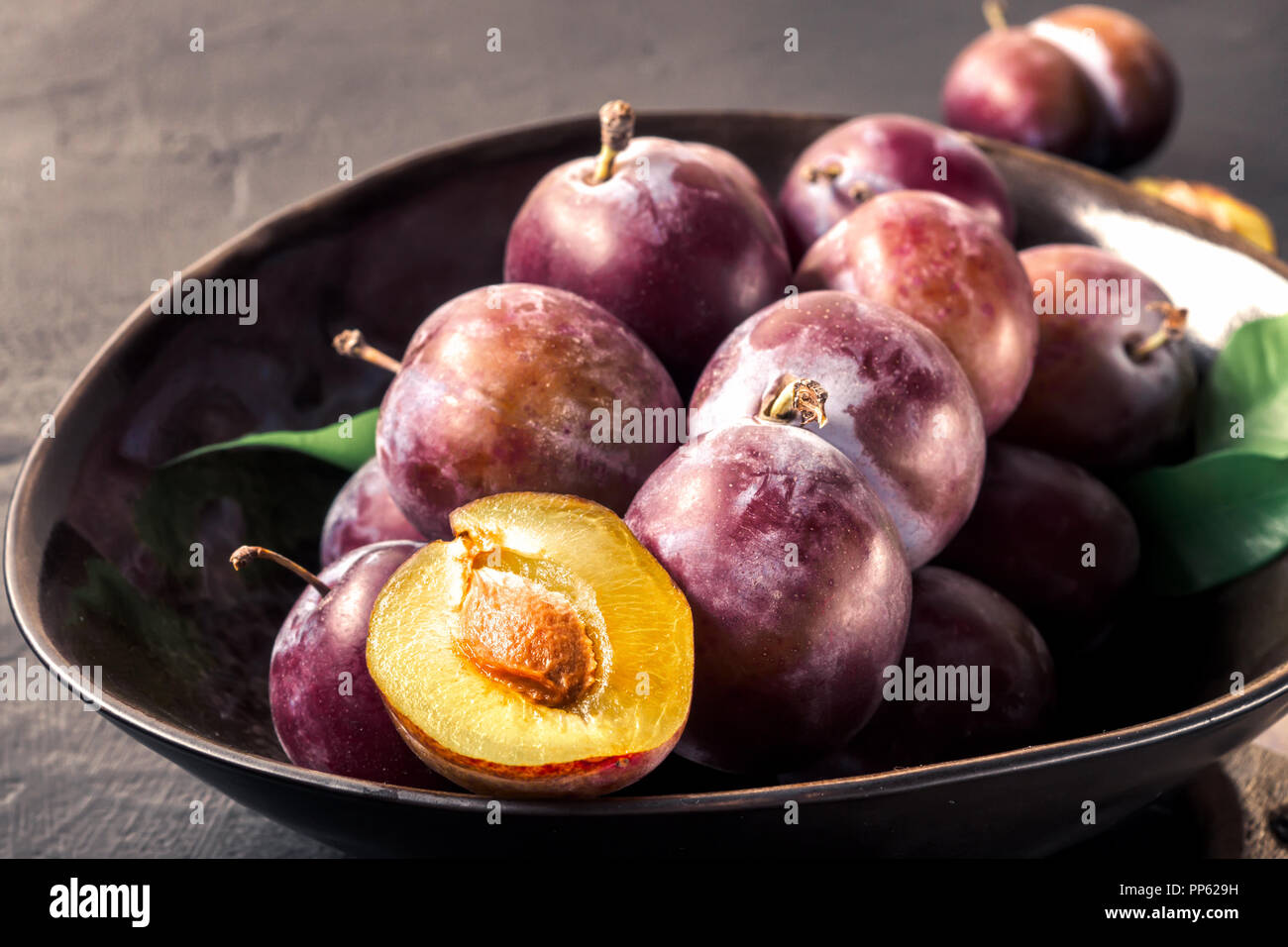 Whole fresh red violet blue plums and slices cut with knife in bowl on ...