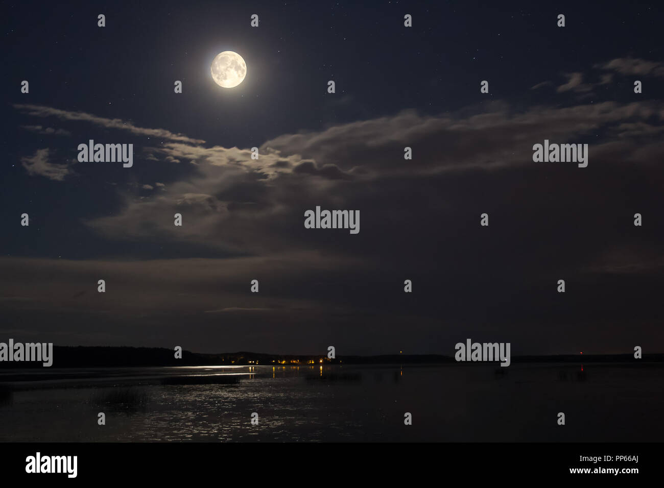 Cloudy weather in summer, moon in the night sky above lake, in Riga ...