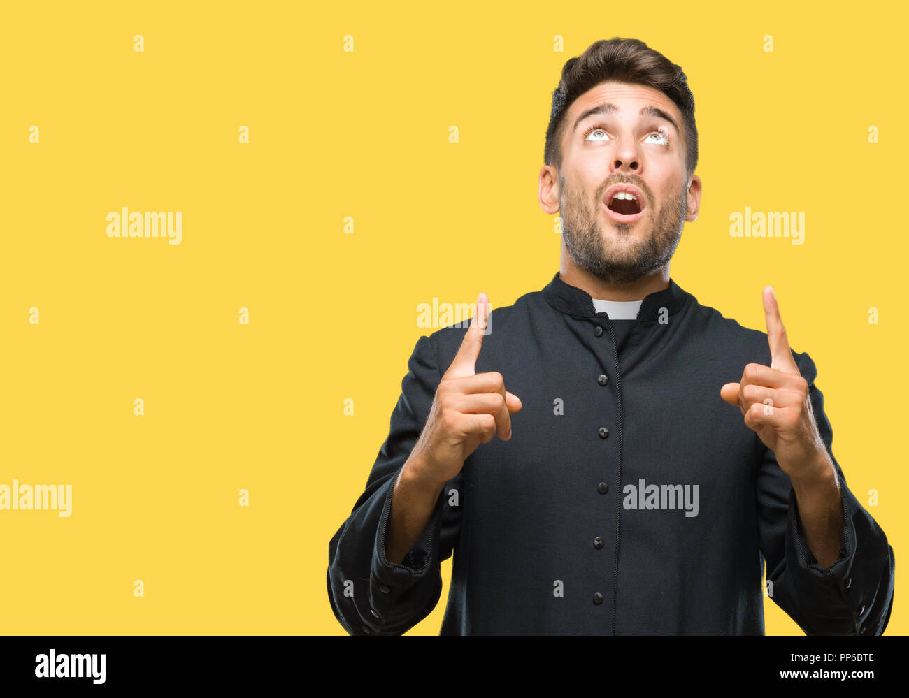 Young catholic christian priest man over isolated background amazed and ...