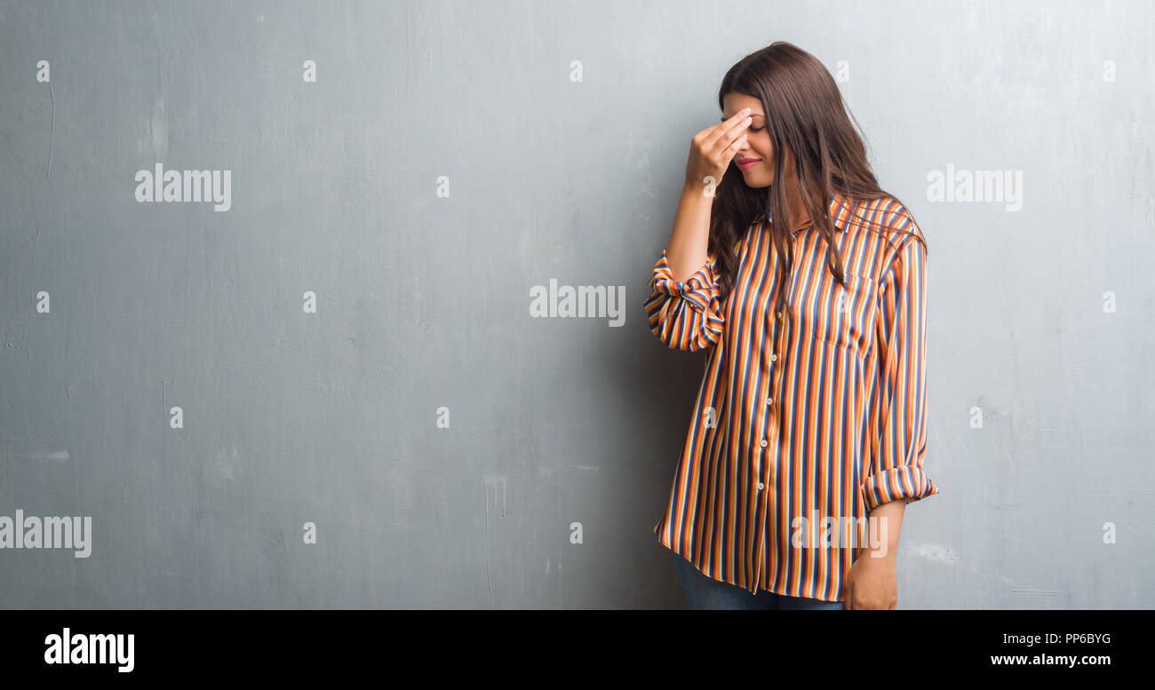 Young brunette woman over grunge grey wall tired rubbing nose and eyes ...