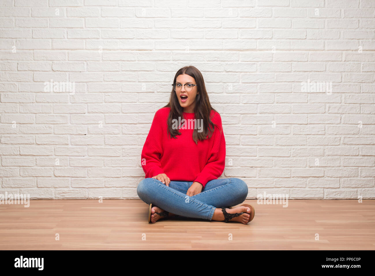 Young Brunette Woman Sitting On The Floor Over White Brick Wall Scared