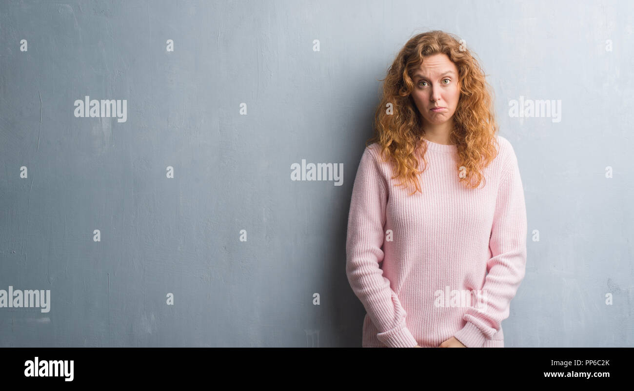 Young redhead woman over grey grunge wall wearing pink sweater ...