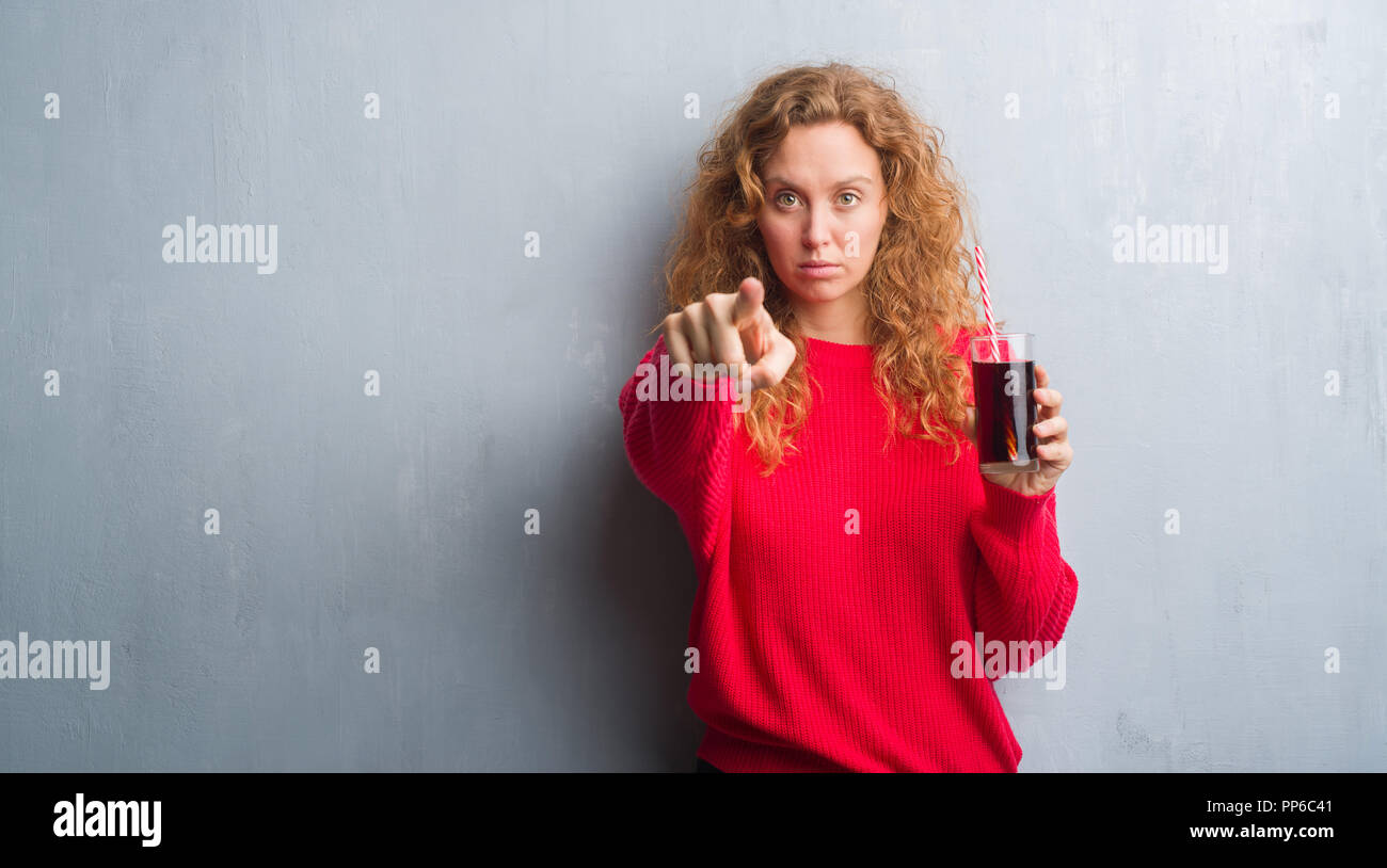 Young redhead woman over grey grunge wall drinking soda refreshment ...